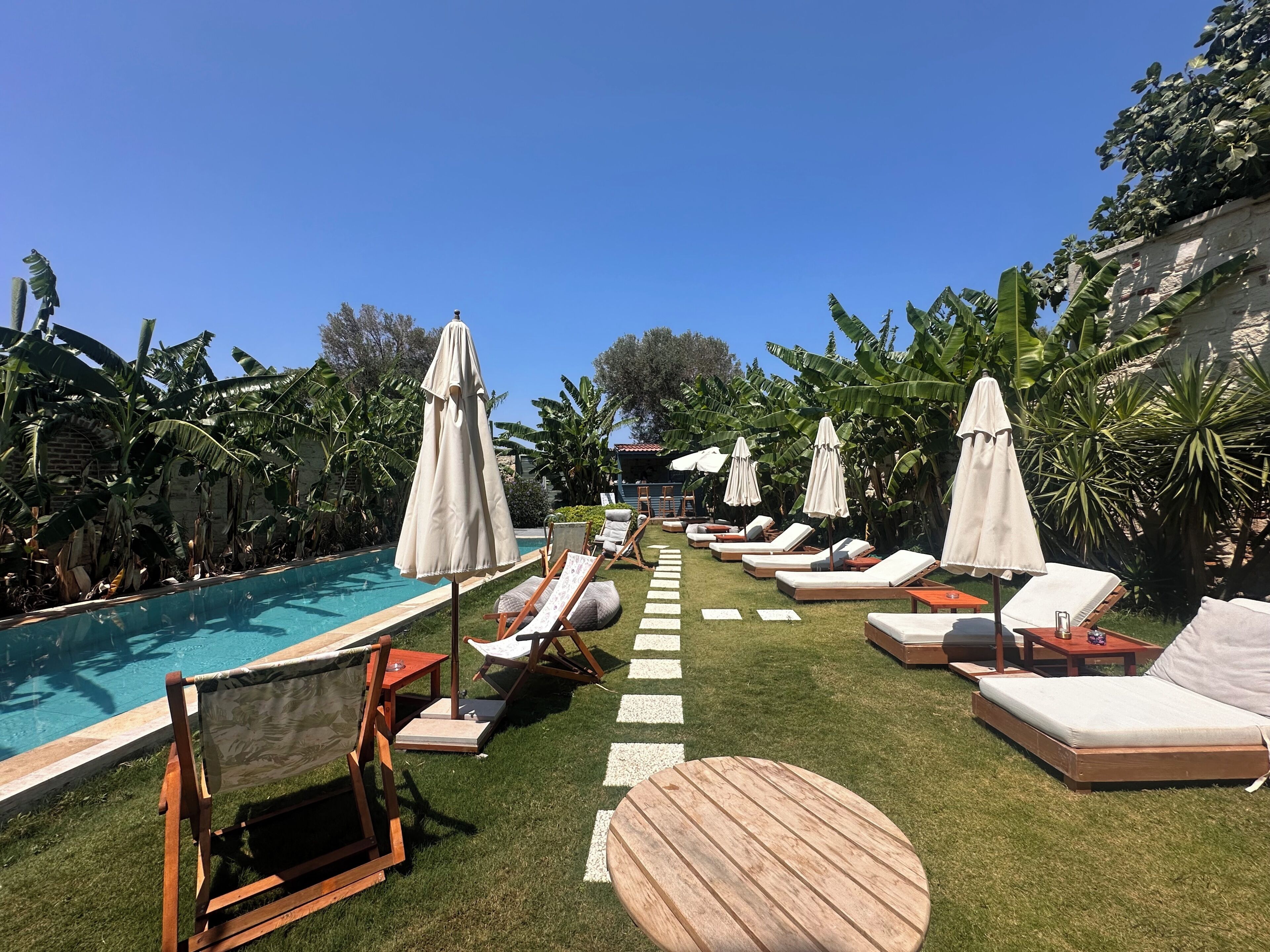 Uma área ao lado da piscina com espreguiçadeiras e guarda-sóis, cercada por vegetação exuberante.