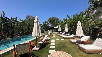 Uma área ao lado da piscina com espreguiçadeiras e guarda-sóis, cercada por vegetação exuberante.