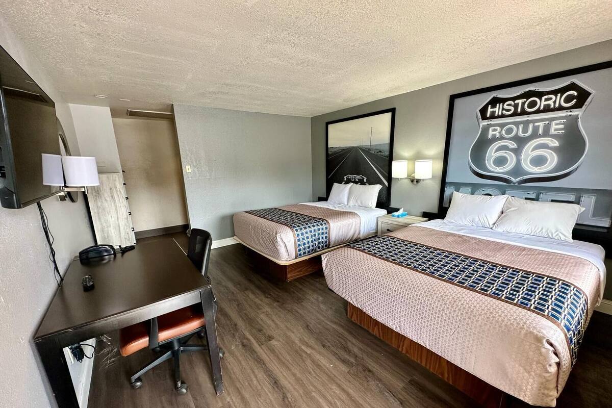 Quarto de hotel com duas camas, uma escrivaninha e uma cadeira. Um letreiro fixado na parede indica "Historic Route 66".