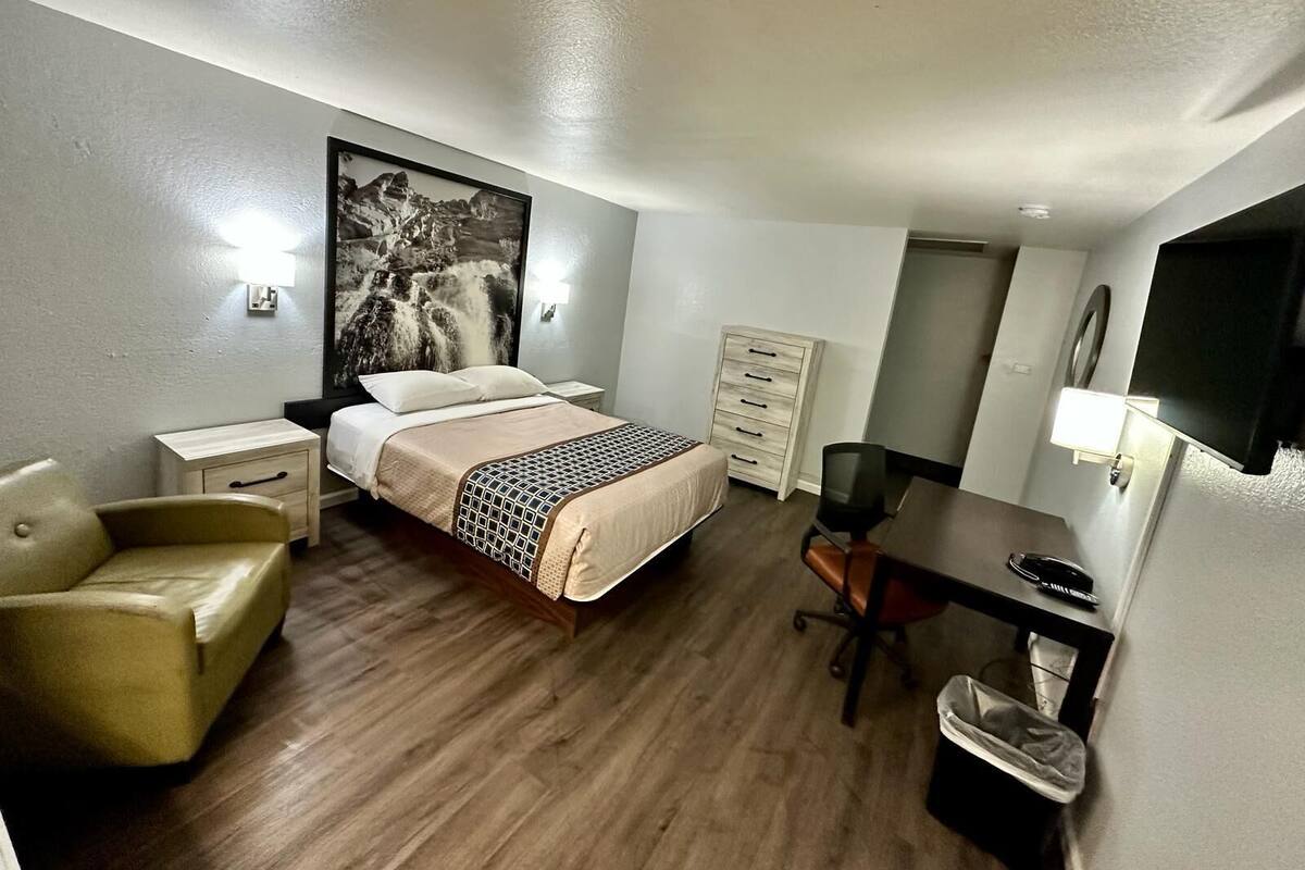 Quarto de hotel com cama, escrivaninha, cadeira, cômoda e televisão.