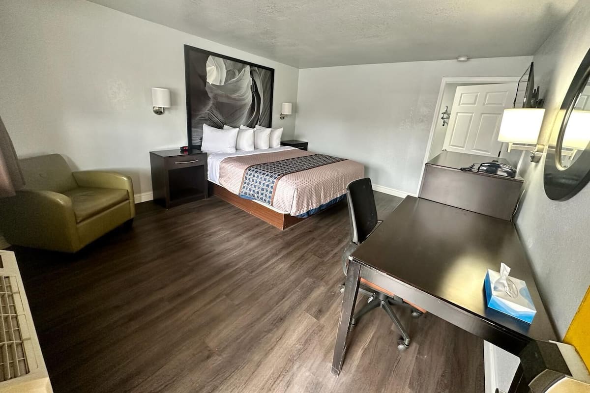 Quarto de hotel com cama, escrivaninha, cadeira, mesa de cabeceira e abajur.
