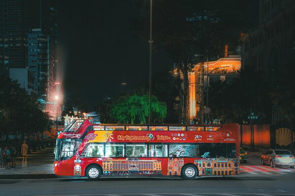 Um ônibus de dois andares bem iluminado, com a marca 'CitySightseeing', trafegando em uma rua da cidade à noite.