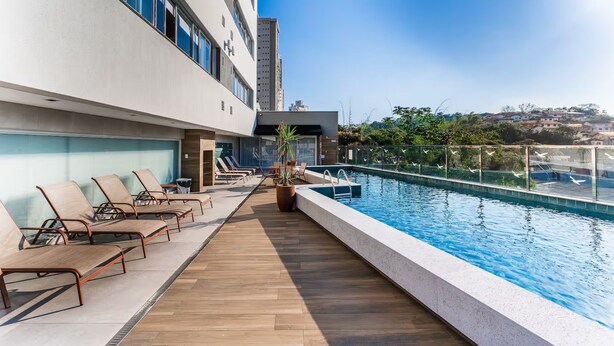 Área de piscina no terraço com espreguiçadeiras e vista da cidade.