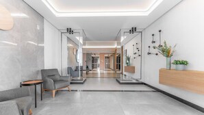 Um hall moderno com divisória de vidro, assentos cinzentos e balcão de recepção em madeira.