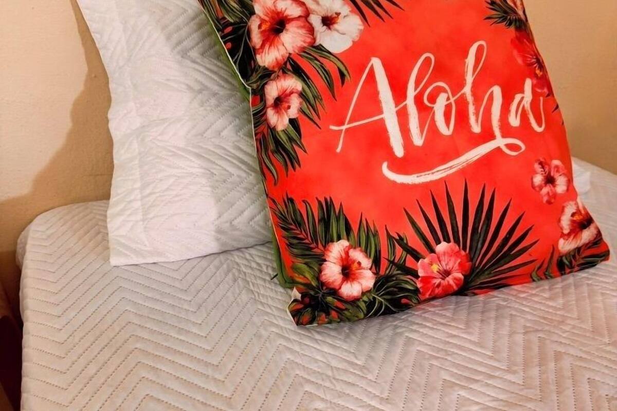 Uma cama com um travesseiro branco e um travesseiro vermelho com a palavra 'Aloha' escrita.
