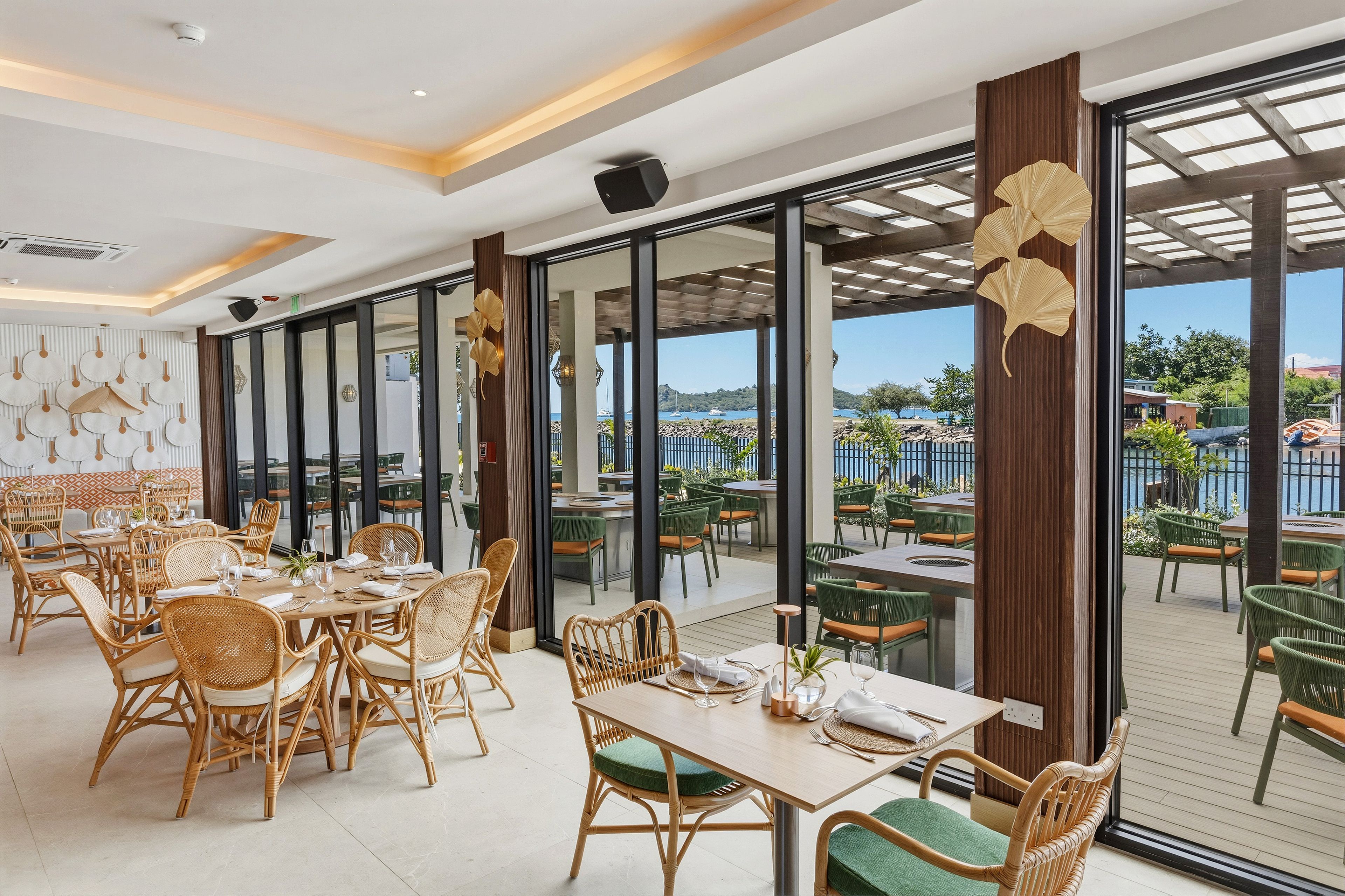 Restaurante com mesas dentro e fora, grandes janelas e vista para o mar.