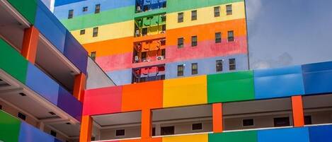 Um hotel com vários andares, fachada colorida e área de piscina com espreguiçadeiras.