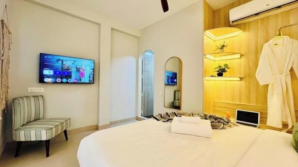 Quarto de hotel com uma cama grande, televisão presa na parede, área de estar com uma cadeira e um roupão pendurado em um gancho.