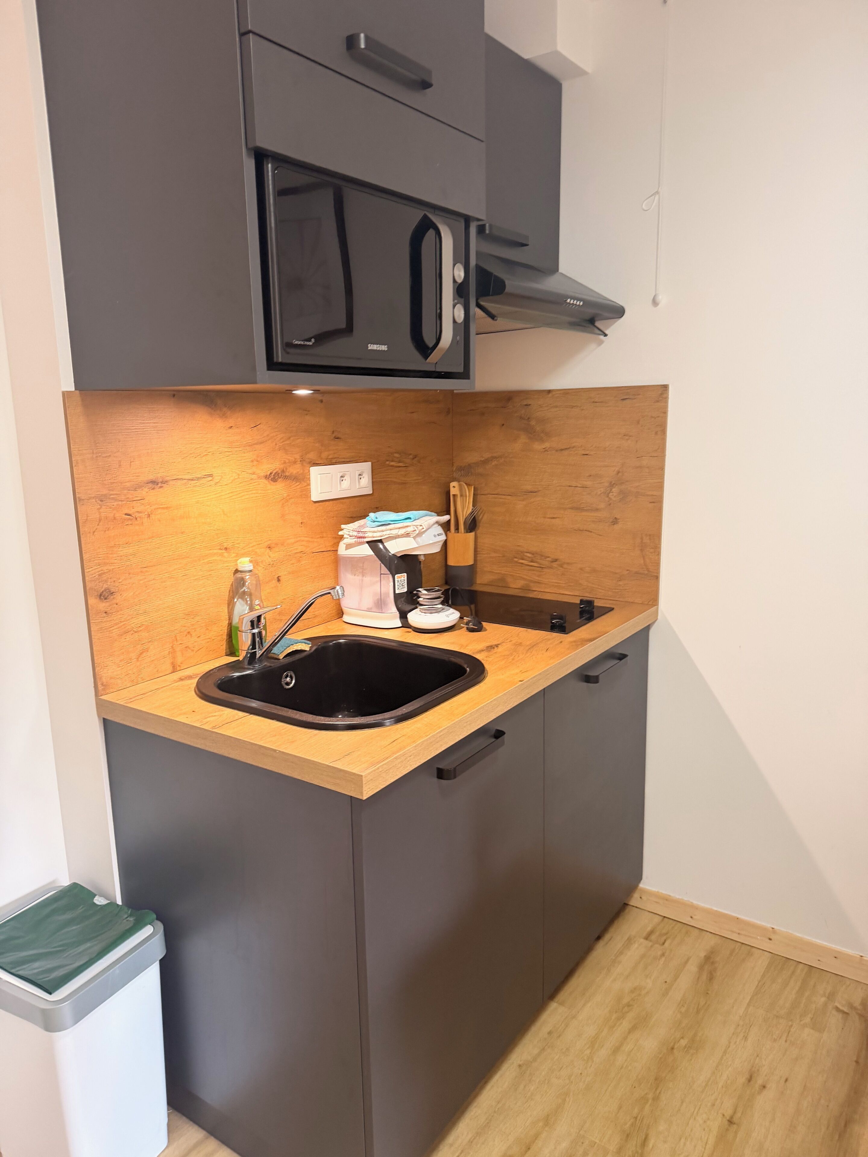 Uma cozinha compacta com micro-ondas embutido, pia com torneira e bancada de madeira.