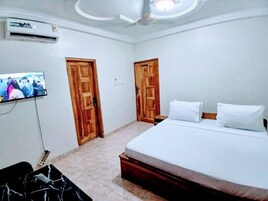 Um quarto com cama, duas portas de madeira, televisão e aparelho de ar condicionado.