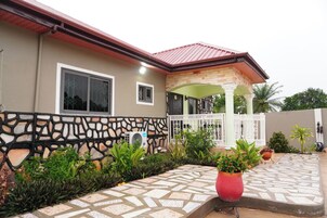Uma casa com fachada de pedra, um pátio com azulejos e um alpendre coberto.