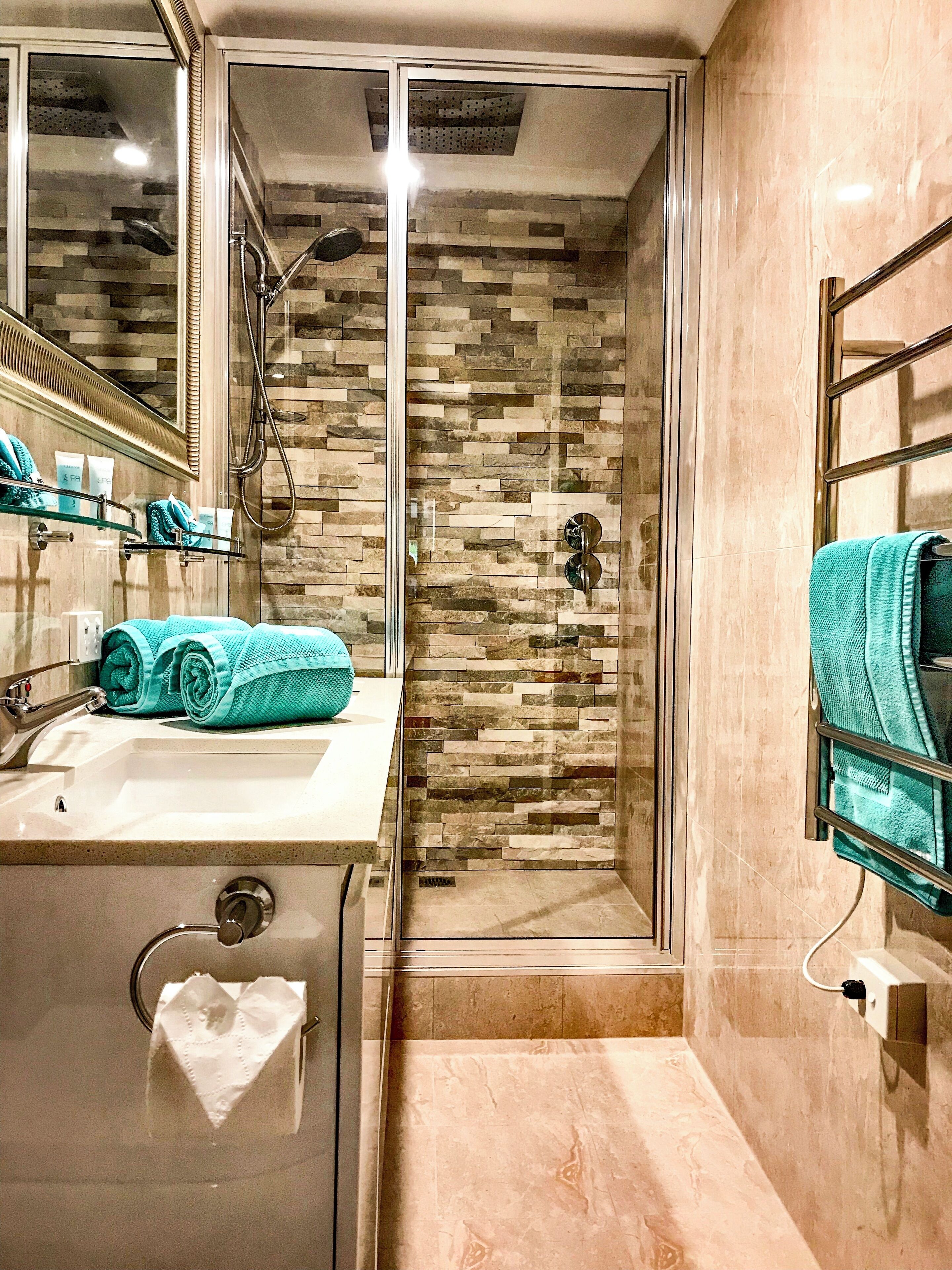 Uma casa de banho moderna com chuveiro de vidro, lavatório de mármore e um porta-toalhas com uma toalha enrolada.