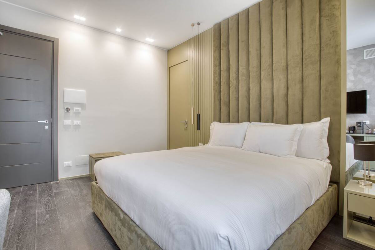 Quarto moderno com cama grande, guarda-roupa, mesa de cabeceira e televisão na parede.