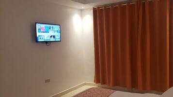 Quarto de hotel com cama, televisão fixada na parede e janela com cortinas.