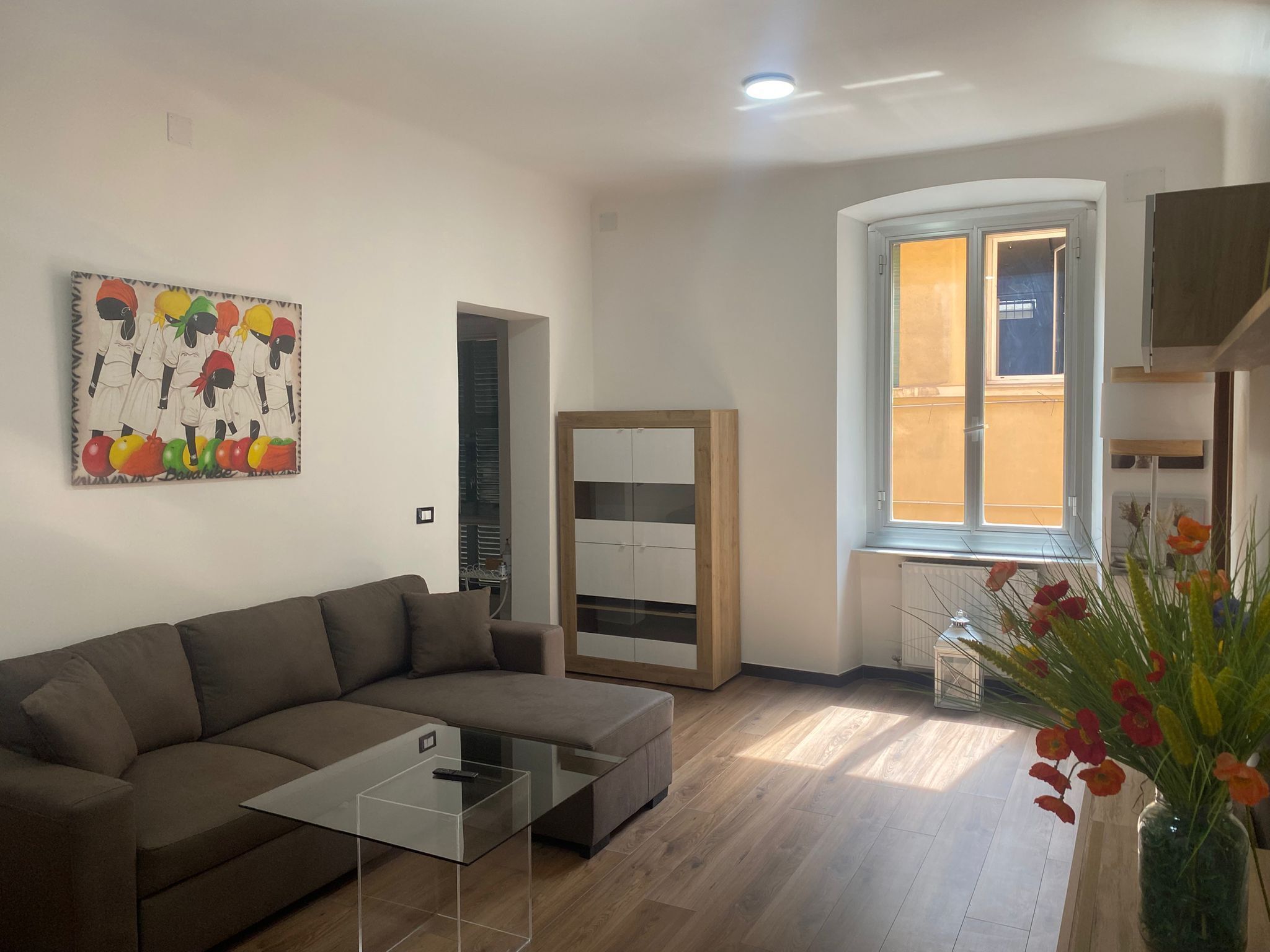 Uma sala de estar moderna com um sofá seccional marrom, uma mesa de centro de vidro, um armário de madeira e uma janela grande com vista para o exterior.