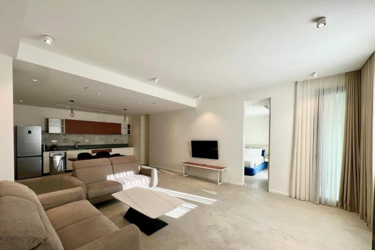Uma sala de estar moderna com sofá, televisão de tela plana e cozinha ao fundo.