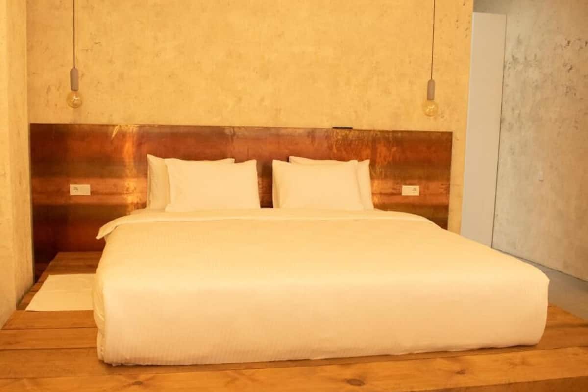 Uma cama com cabeceira de madeira, roupa de cama branca e duas luminárias laterais.