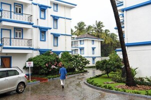 Um edifício residencial com detalhes azuis e varandas, um acesso molhado e uma placa indicando área proibido estacionar.