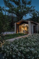 Um edifício moderno com área de recepção, rodeado por vegetação exuberante e flores brancas.