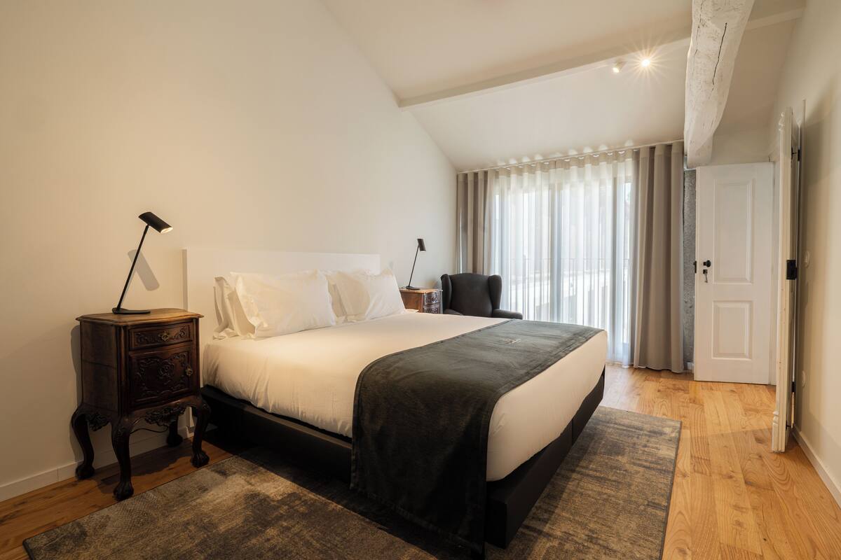 Quarto com cama grande, mesa de cabeceira, uma cadeira e porta.