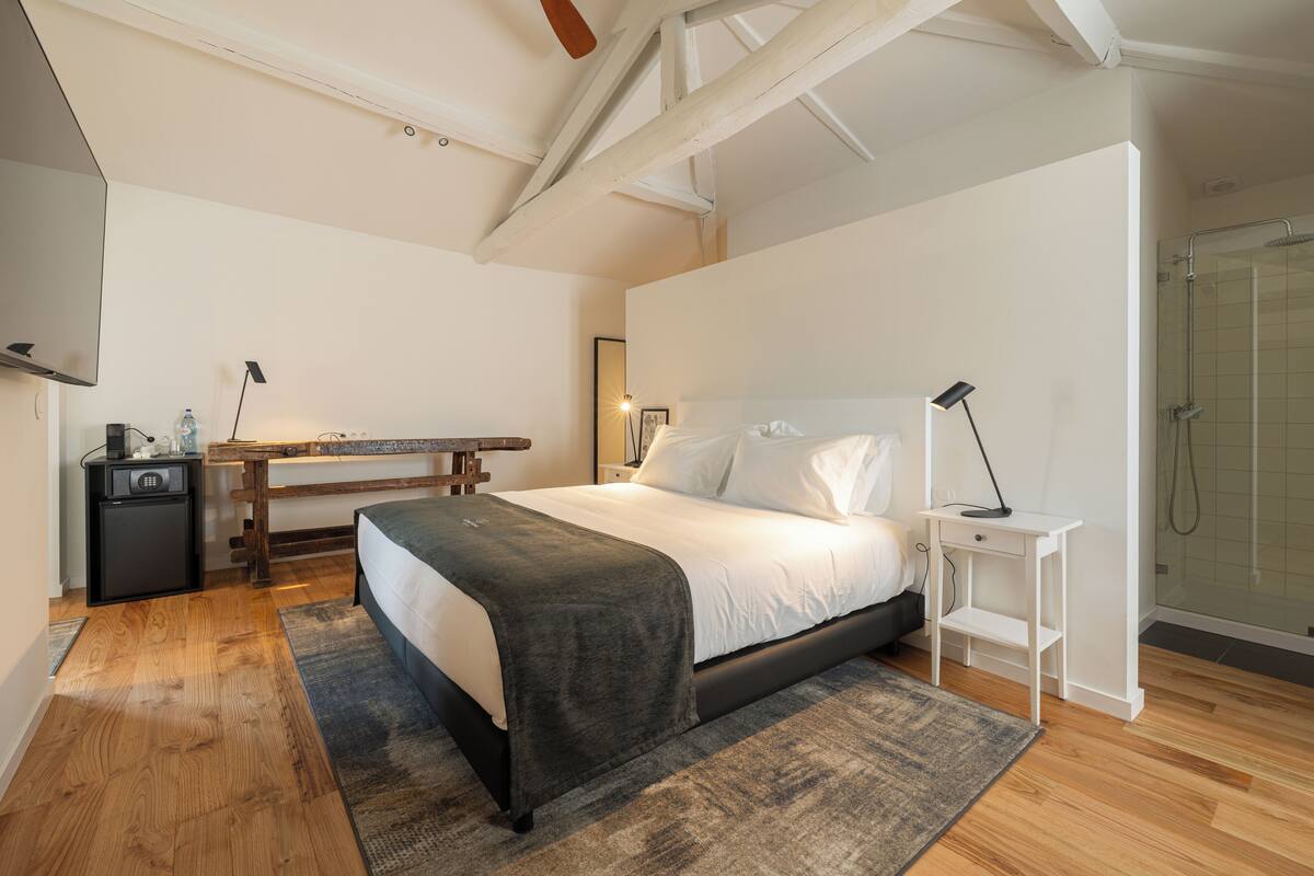 Quarto com cama, mesa de cabeceira, escrivaninha e área de chuveiro.