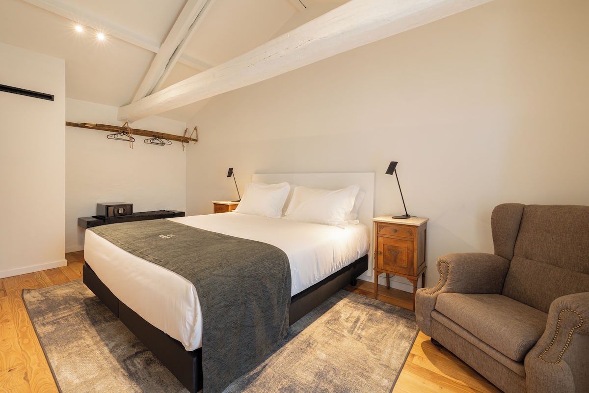 Quarto com cama, mesas de cabeceira, uma cadeira e guarda-roupa.