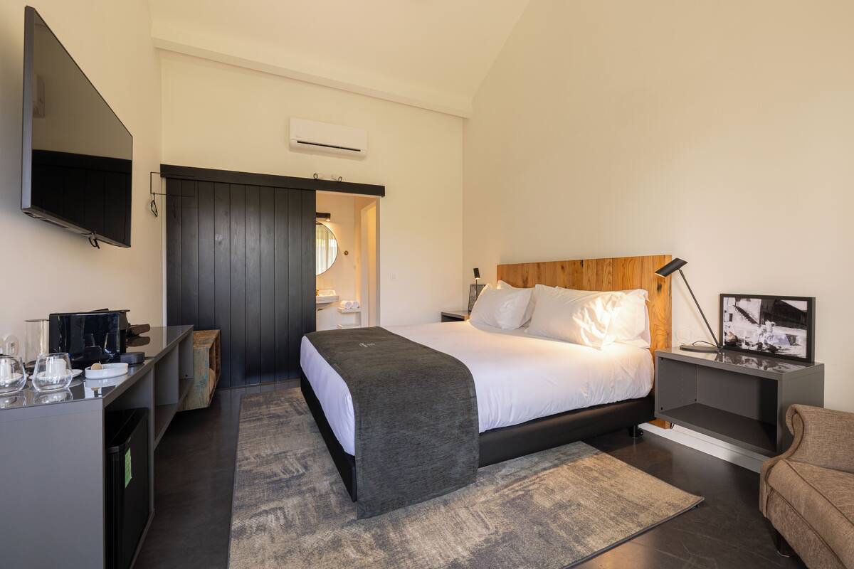 Quarto de hotel moderno com uma cama grande, mesa de cabeceira e televisão na parede.