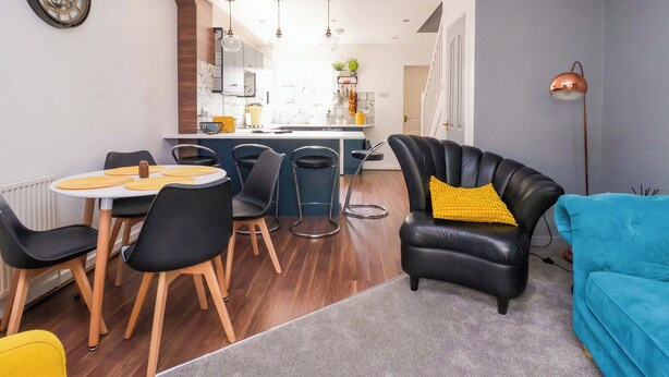 Uma sala de estar moderna com área de jantar, cozinha ao fundo e sofá azul.