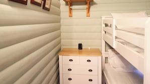 Um quarto pequeno e acolhedor com uma cama beliche, uma mesa de cabeceira de madeira, um armário e quadros nas paredes.