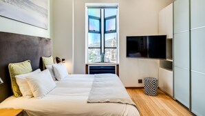 Um quarto moderno com uma cama grande, televisão de tela plana, janela com vista para a cidade e guarda-roupa.