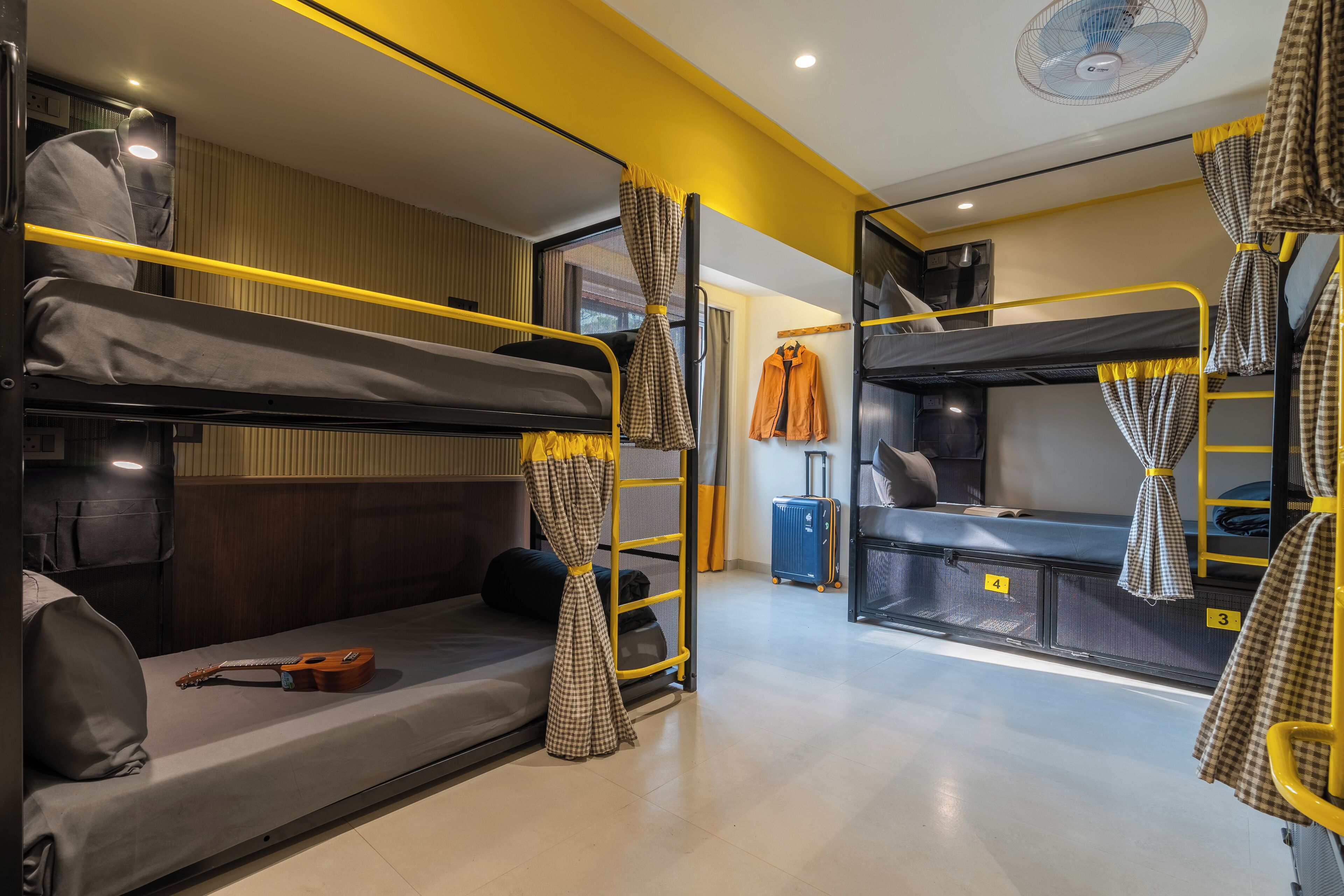 Quarto estilo dormitório com beliches, uma guitarra e uma mala.