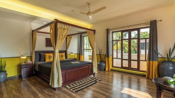 Um quarto espaçoso com cama de dossel, ventilador de teto e amplas janelas com cortinas.