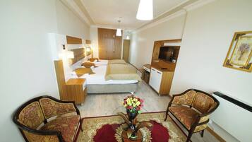 Quarto de hotel pequeno com cama, mesas de cabeceira, televisão, escrivaninha e área de estar com cadeiras e mesa.