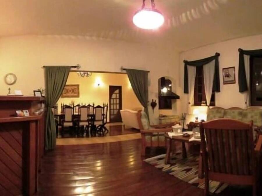 Uma sala de estar espaçosa com piso de madeira, um espaço de jantar com cadeiras e mesa, e um canto aconchegante com sofá e poltronas.
