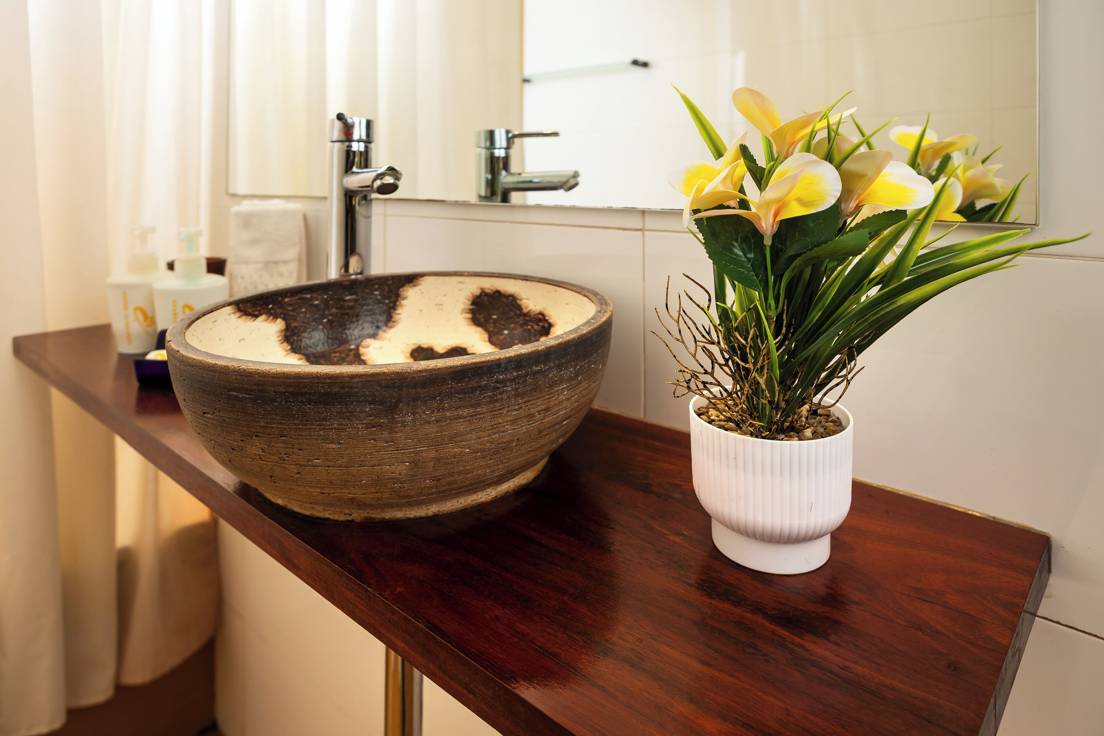 Uma casa de banho com uma grande bacia de cerâmica, uma pia branca e um vaso com flores amarelas.
