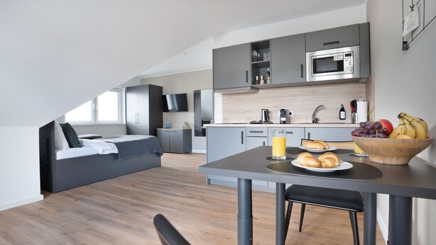 Um apartamento moderno do tipo loft, com área de refeições, cozinha compacta e cama em mezanino.