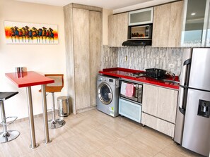 Cozinha compacta com máquina de lavar, micro-ondas e geladeira de aço inoxidável.