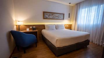 Quarto de hotel com cama, escrivaninha, cadeira, abajur e um quadro na parede.