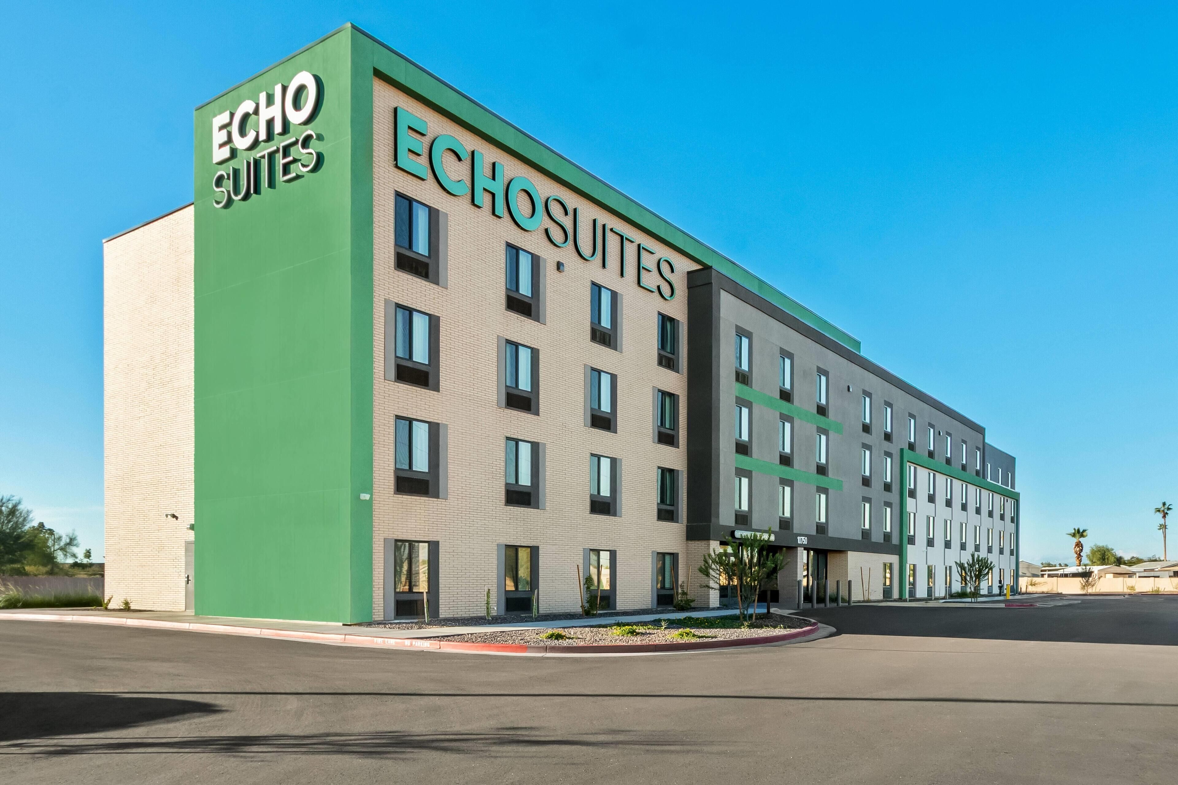 Um hotel chamado ECHO SUITES, com design moderno, apresentando esquema de cores verde e bege, vários andares e um estacionamento à frente.