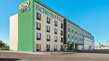 Um hotel chamado ECHO SUITES, com design moderno, apresentando esquema de cores verde e bege, vários andares e um estacionamento à frente.