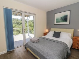 Quarto com cama, mesa de cabeceira, quadro na parede e varanda com vista para o verde.