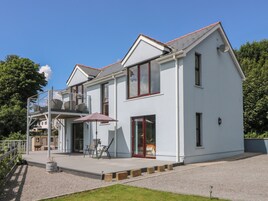 Uma casa de dois andares com varanda, um pátio com mobiliário externo e uma entrada com calçamento de brita.
