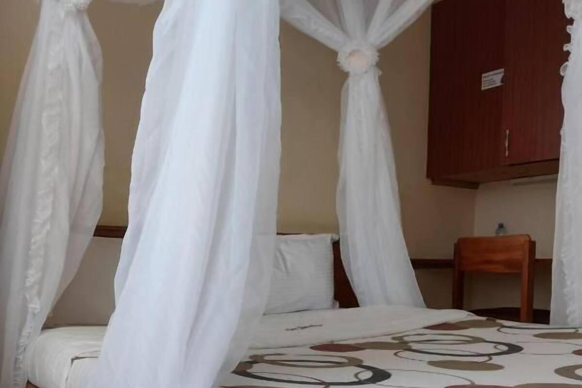 Uma cama de solteiro com dossel, cabeceira de madeira e colcha estampada.