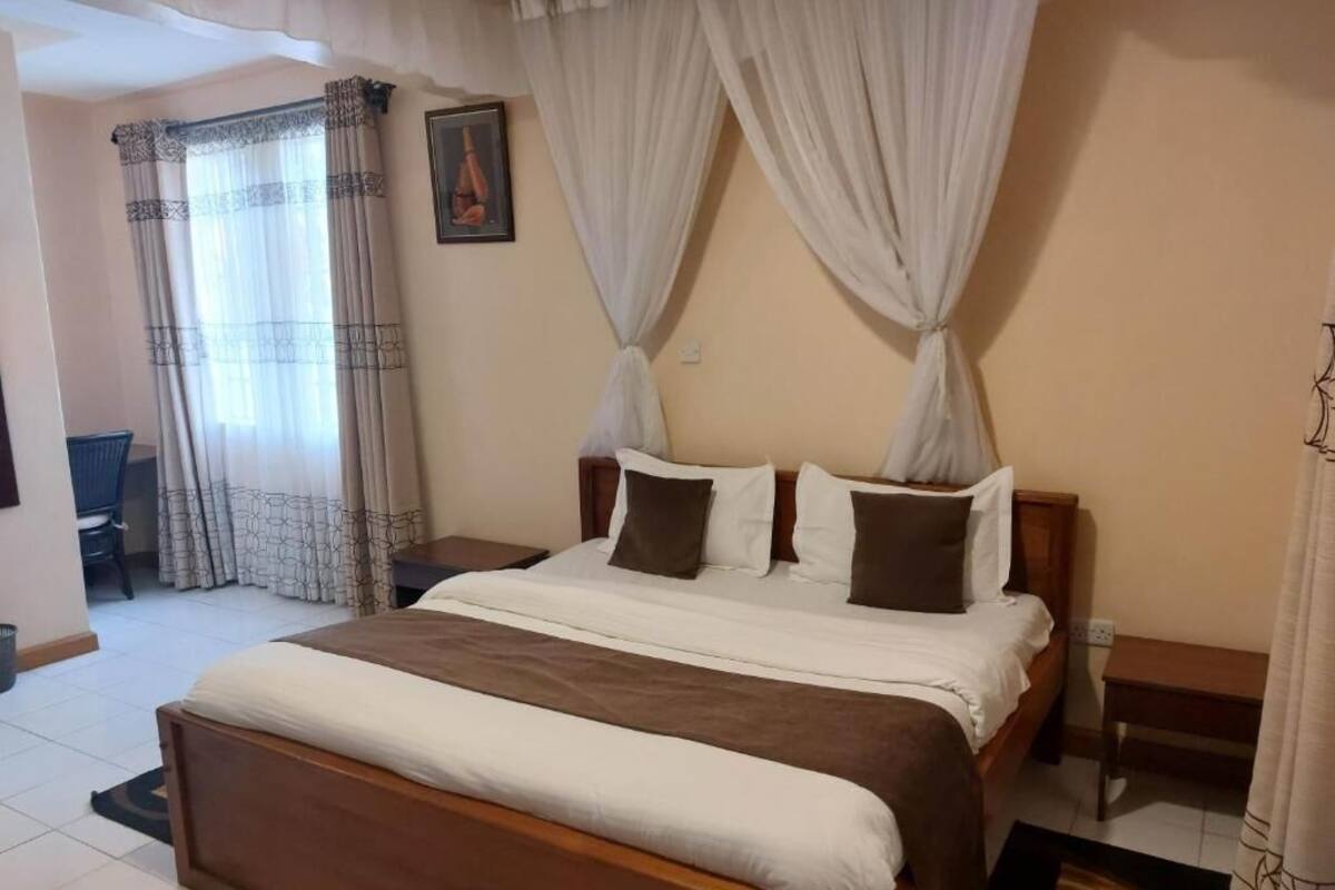 Quarto com uma cama grande, cortinas, escrivaninha e uma cadeira.