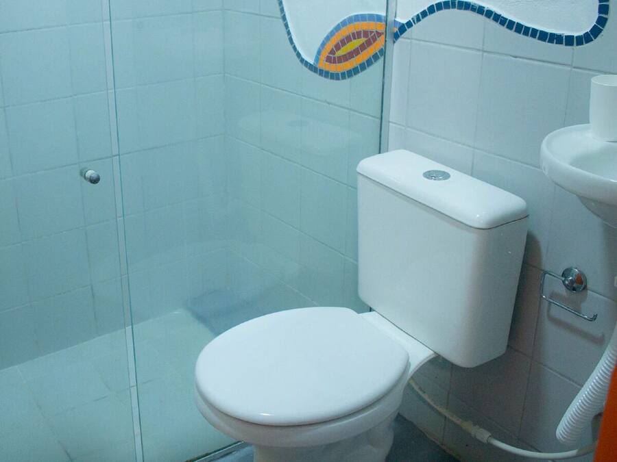 Casa de banho com sanita branca, cabine de duche em vidro e parede revestida com padrão decorativo.