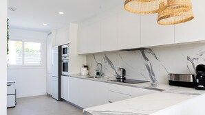 Uma cozinha moderna com armários brancos, painel de fundo de mármore e uma ilha central.