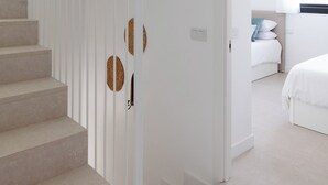 Uma escadaria com corrimãos brancos leva a um quarto com cama e janela.