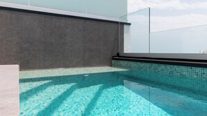 Piscina no terraço com água azul cristalina, rodeada por um guarda-corpo de vidro moderno e uma parede cinzenta.