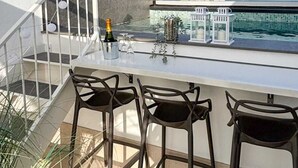 Uma varanda moderna com guarda-corpo de vidro, espaço de bar com banquetas e vista para o oceano.