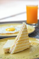 Sanduíche em um prato, com um copo de suco de laranja ao fundo.